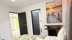 Quarto de hotel com uma cama, uma pintura do pôr do sol e um ventilador de teto.