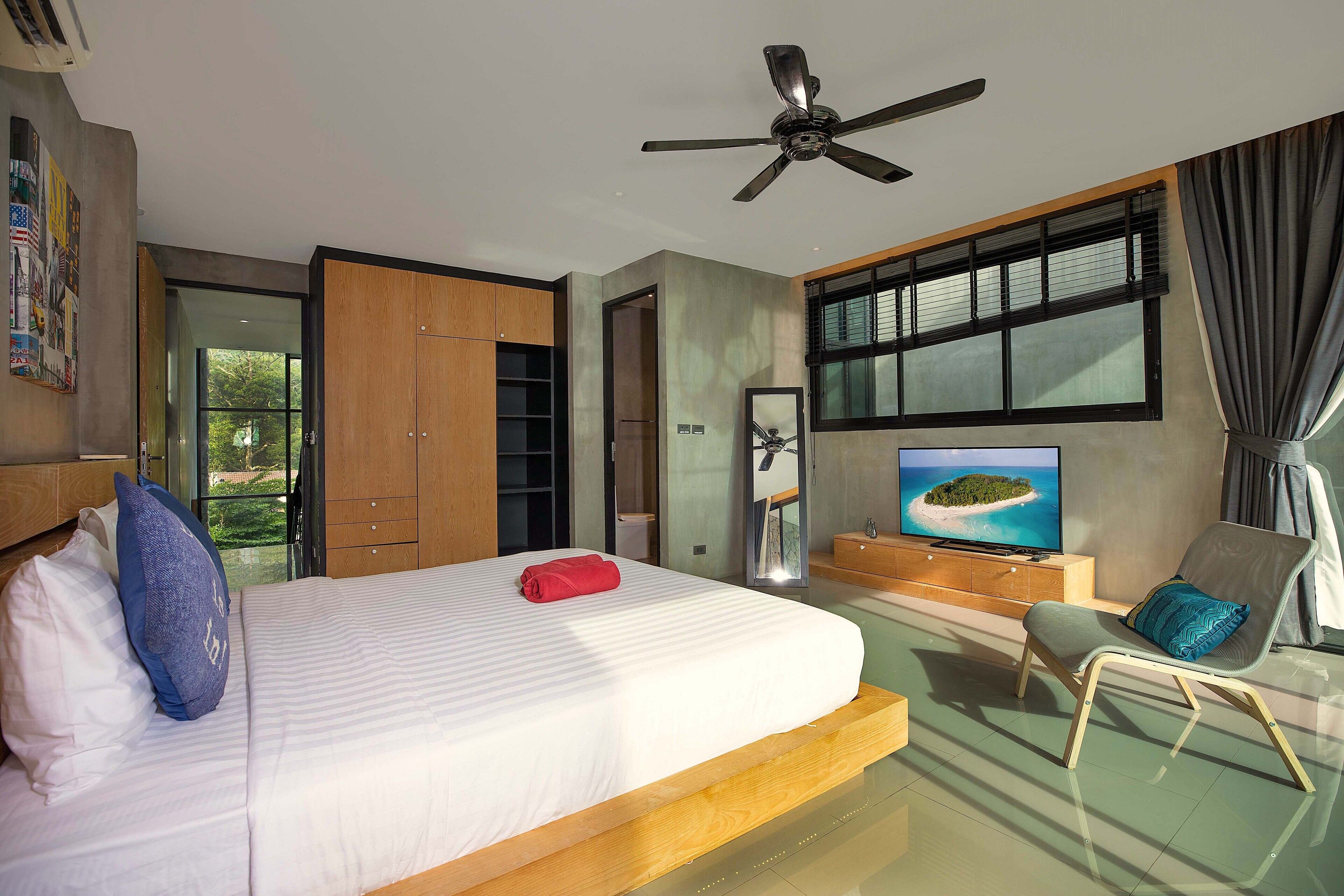 Quarto de hotel moderno com uma cama grande, televisão, ventoinha no teto e vista para o exterior.