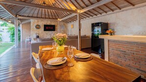 Uma sala de jantar com uma mesa de madeira posta para quatro pessoas, um vaso amarelo com flores e uma placa da Netflix na parede.