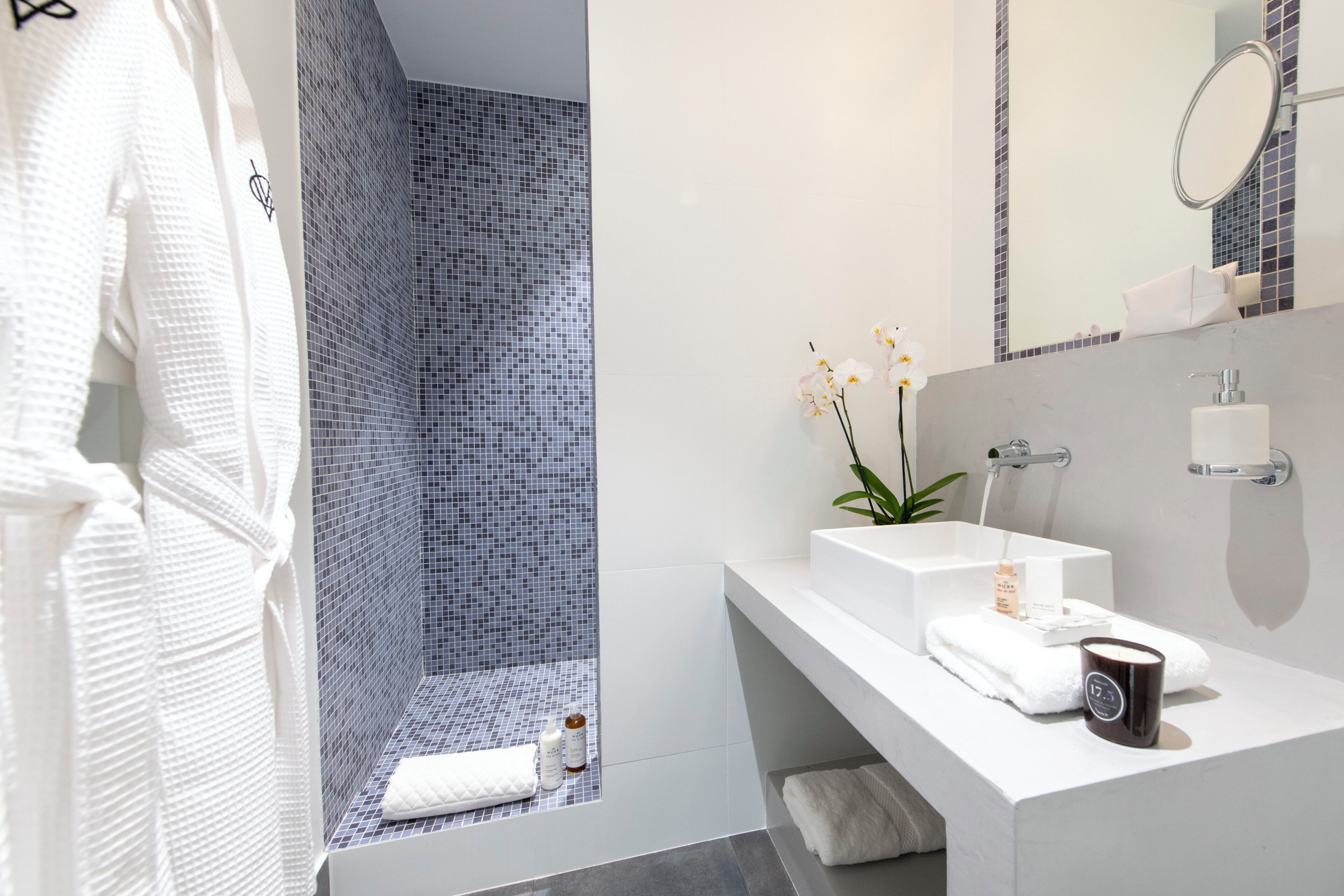 Um banheiro moderno com toucador branco, um espelho grande e área de chuveiro com azulejos de mosaico azuis.