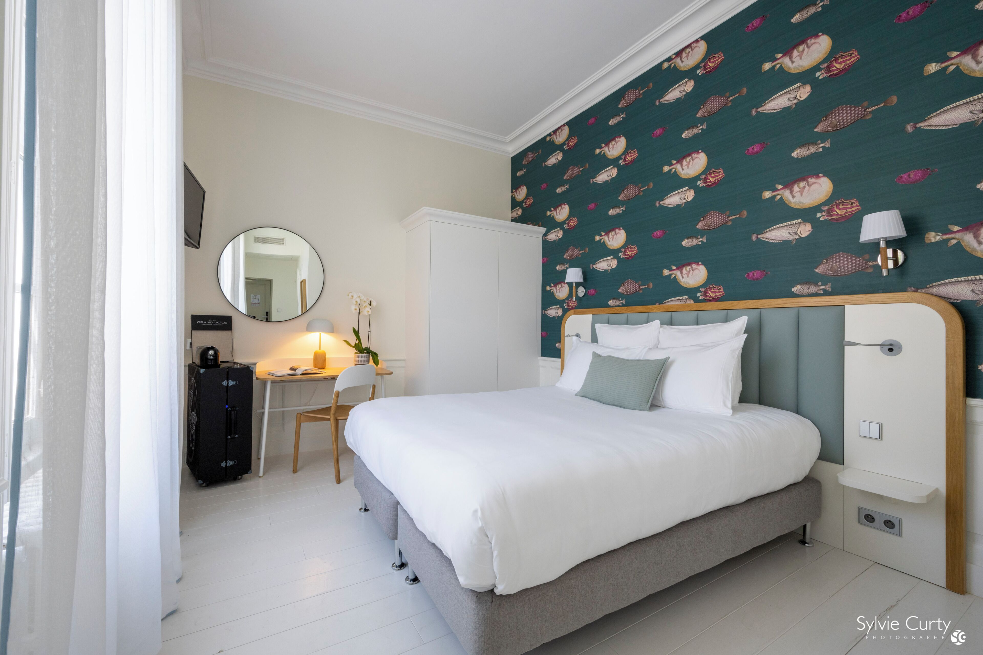 Quarto de hotel com cama, escrivaninha, cadeira e espelho.