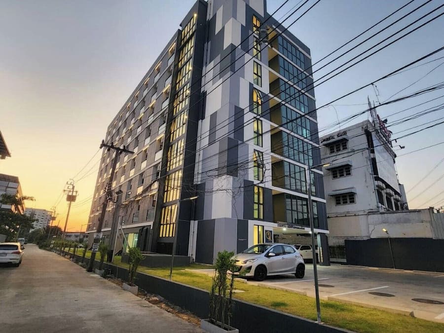 Um edifício moderno com vários andares, janelas amplas e uma área de estacionamento com carros.