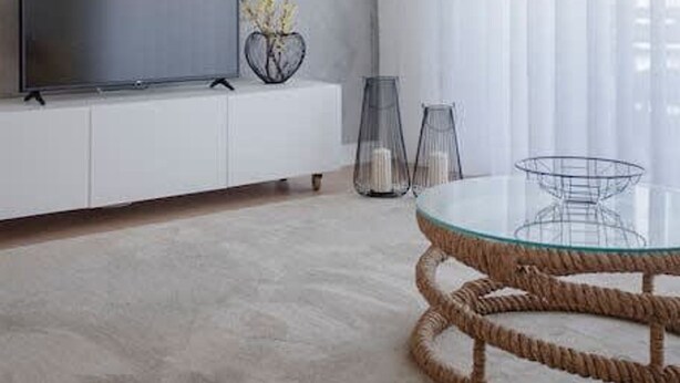 Uma sala de estar moderna com uma TV de tela plana, uma mesa de vidro redonda e um sofá branco.