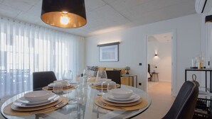 Uma área de refeições moderna com uma mesa de vidro redonda posta para quatro pessoas, pratos brancos e copos de vidro transparente.