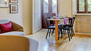 Uma sala de jantar com uma mesa posta para quatro pessoas, um sofá e quadros nas paredes.