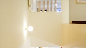 Um interior moderno com uma escada para um segundo andar, uma sala de jantar com mesa e cadeiras, e um pequeno espaço de estar com sofá e planta.