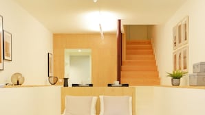 Quarto moderno com cama, cabeceira de madeira, uma mesinha com uma xícara e uma planta, e escada que leva a outro cômodo.