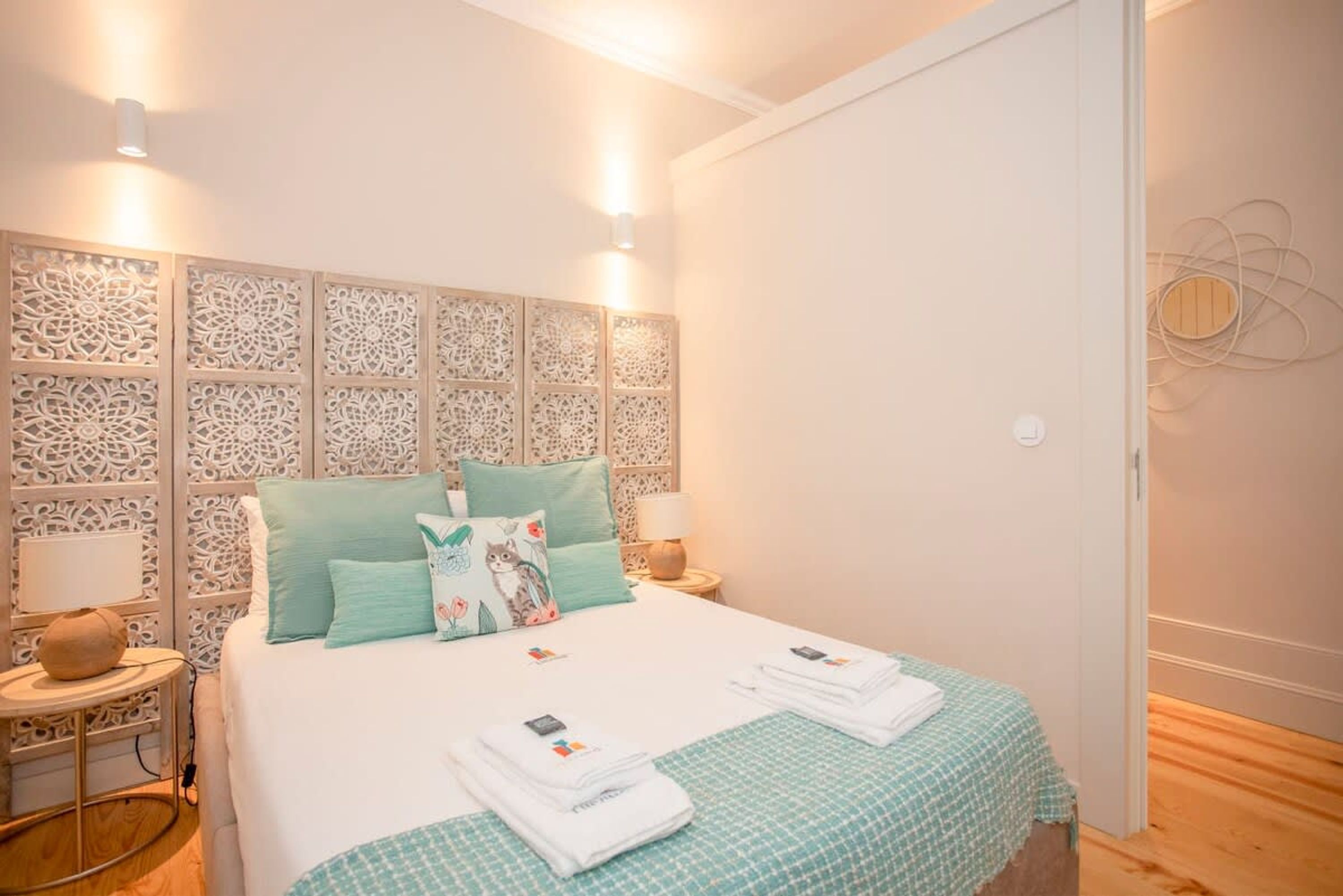 Cama bem arrumada com roupa de cama verde, cabeceira decorativa e mesa de cabeceira com abajur.