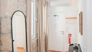 Um corredor com parede de pedra, espelho, porta com extintor e uma pequena mesa com velas.