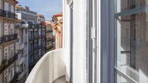 Varanda estreita com fachada branca, com vista para uma rua com edifícios altos.
