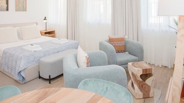 Quarto de hotel moderno com uma cama, duas poltronas, uma mesinha e uma mesa de cabeceira.