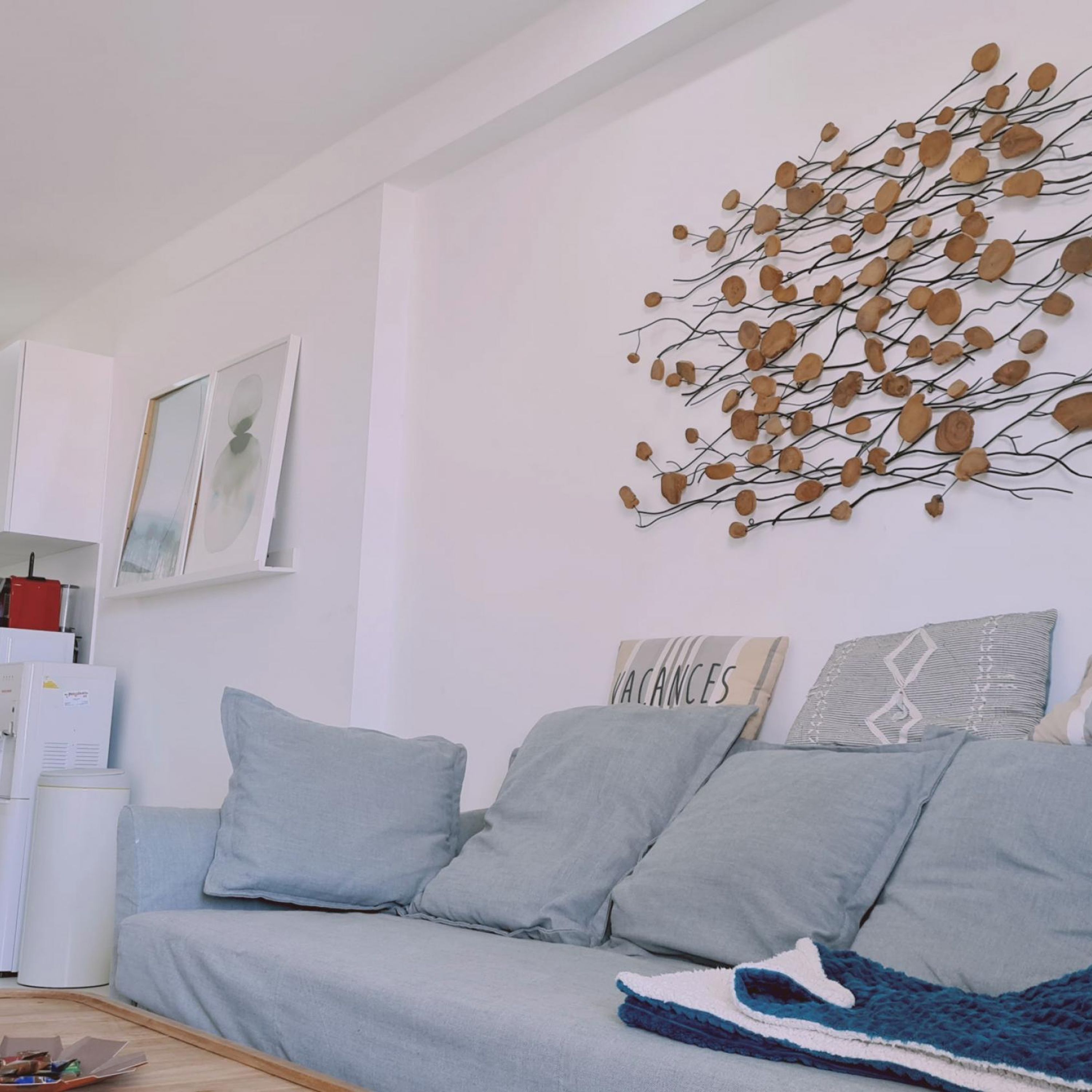 Uma sala de estar moderna com um sofá cinzento, um objeto decorativo na parede e uma placa com a palavra 'VACANCES'.