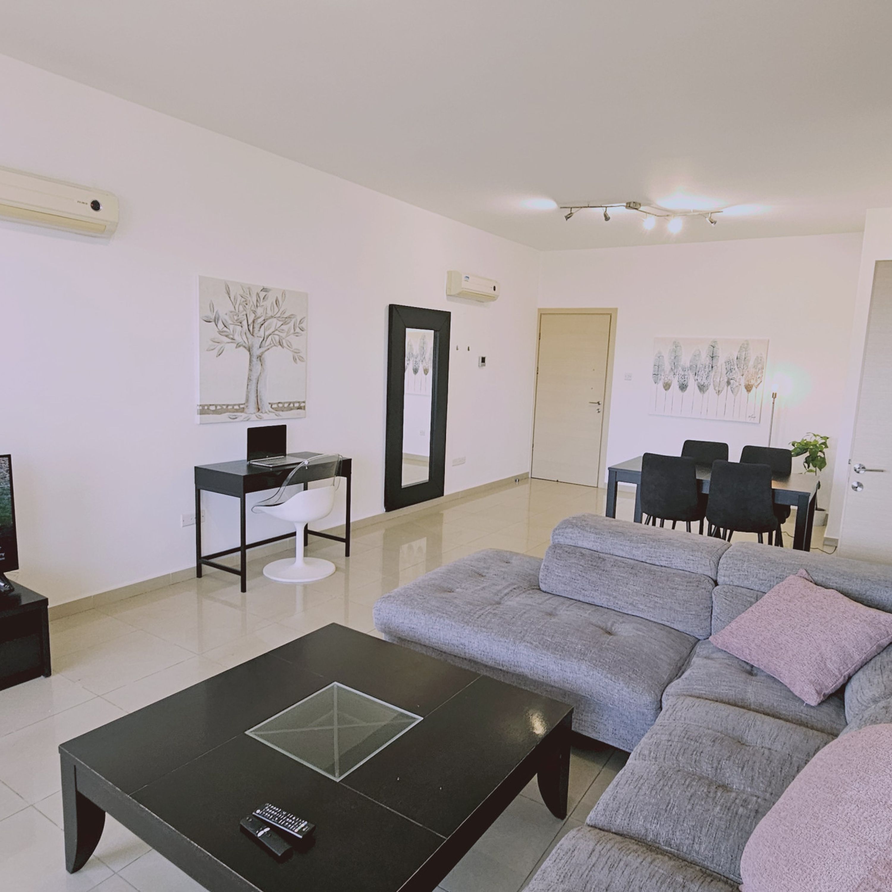 Uma sala de estar moderna com um sofá cinza, uma mesa de centro preta e um espaço de jantar com mesa e cadeiras.