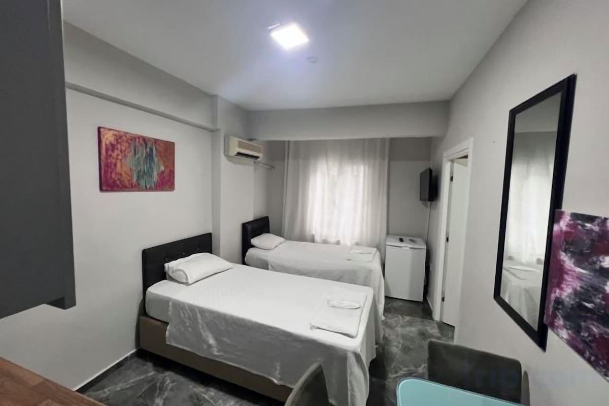 Quarto de hotel com duas camas, uma escrivaninha, uma cadeira, uma televisão e um banheiro.