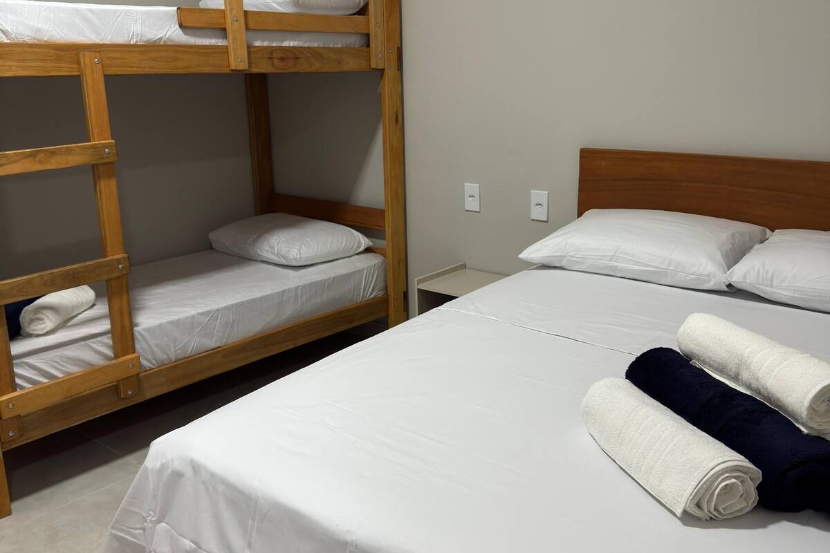 Uma cama de solteiro com roupa de cama branca e uma cama beliche com roupa de cama branca. Há toalhas sobre as camas.