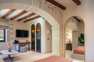 Um quarto espaçoso com uma cama grande, área de estar com mesa e cadeiras, e televisão fixada na parede.