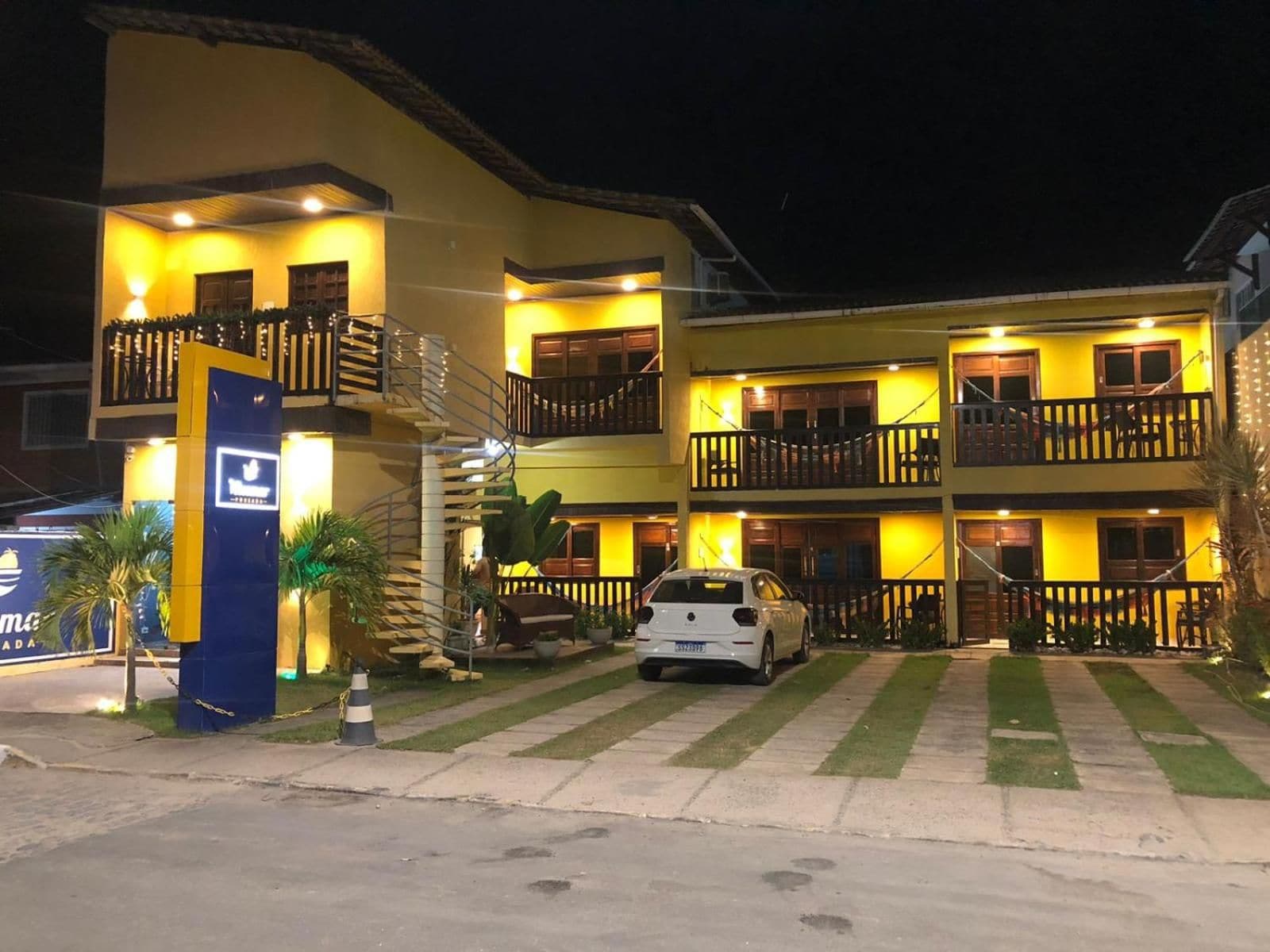 Um hotel de vários andares com varandas, área de estacionamento e uma placa.