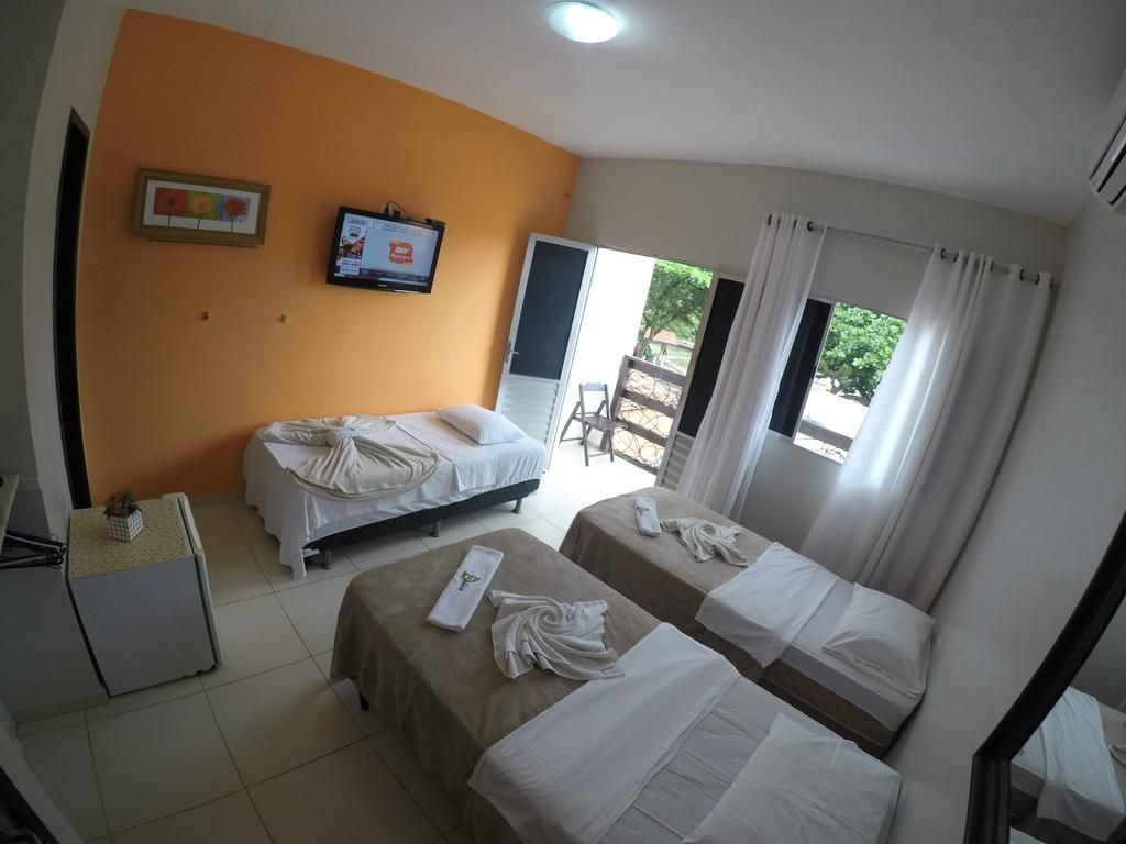 Quarto de hotel com duas camas, televisão, mesa pequena e janela com cortinas.