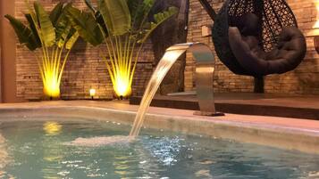 Piscina com um recurso aquático, cercada por plantas e uma cadeira suspensa.
