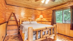 Quarto de cabana de madeira com cama, escada, janela com cortinas e ventilador de teto.