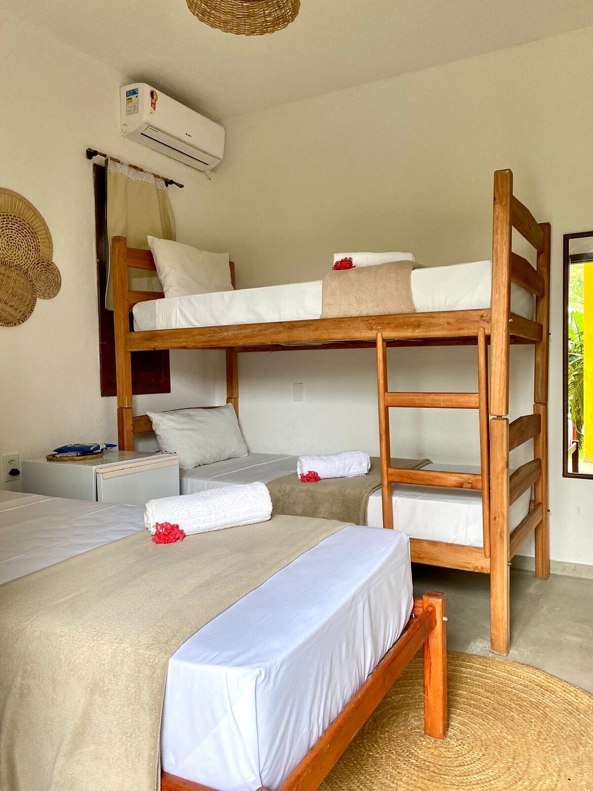Quarto com beliche, um ventilador de teto, uma pequena mesa com uma bolsa e uma cesta de palha na parede.