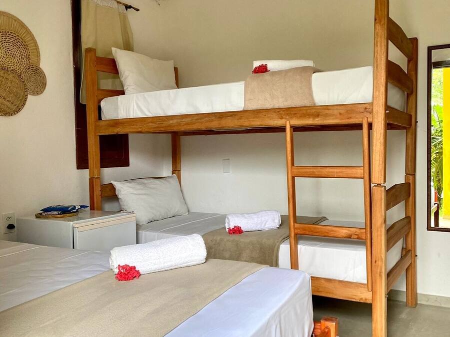 Quarto com beliche, um ventilador de teto, uma pequena mesa com uma bolsa e uma cesta de palha na parede.