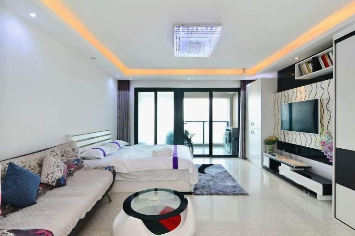 Quarto de hotel moderno com uma cama grande, um sofá, uma mesa de centro, uma TV e uma varanda com vista.