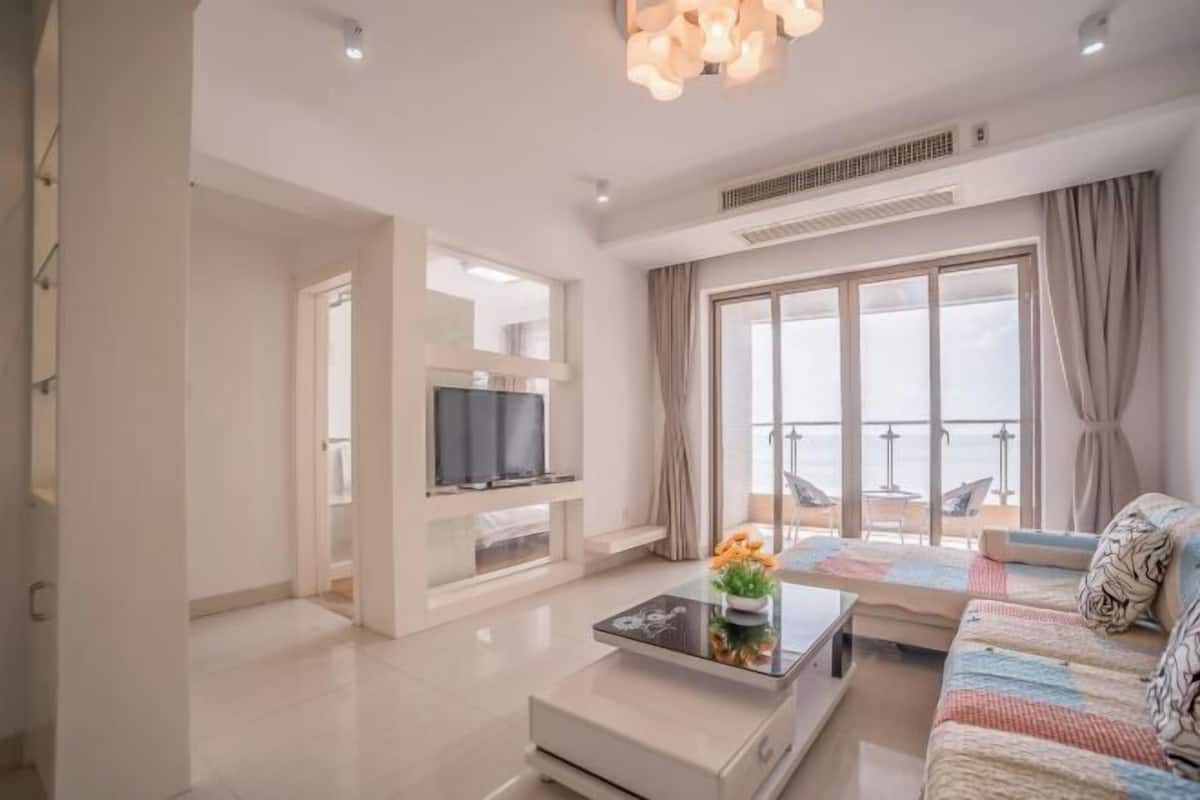 Uma sala de estar moderna com televisão de tela plana, sofá, mesa de centro e varanda com vista.