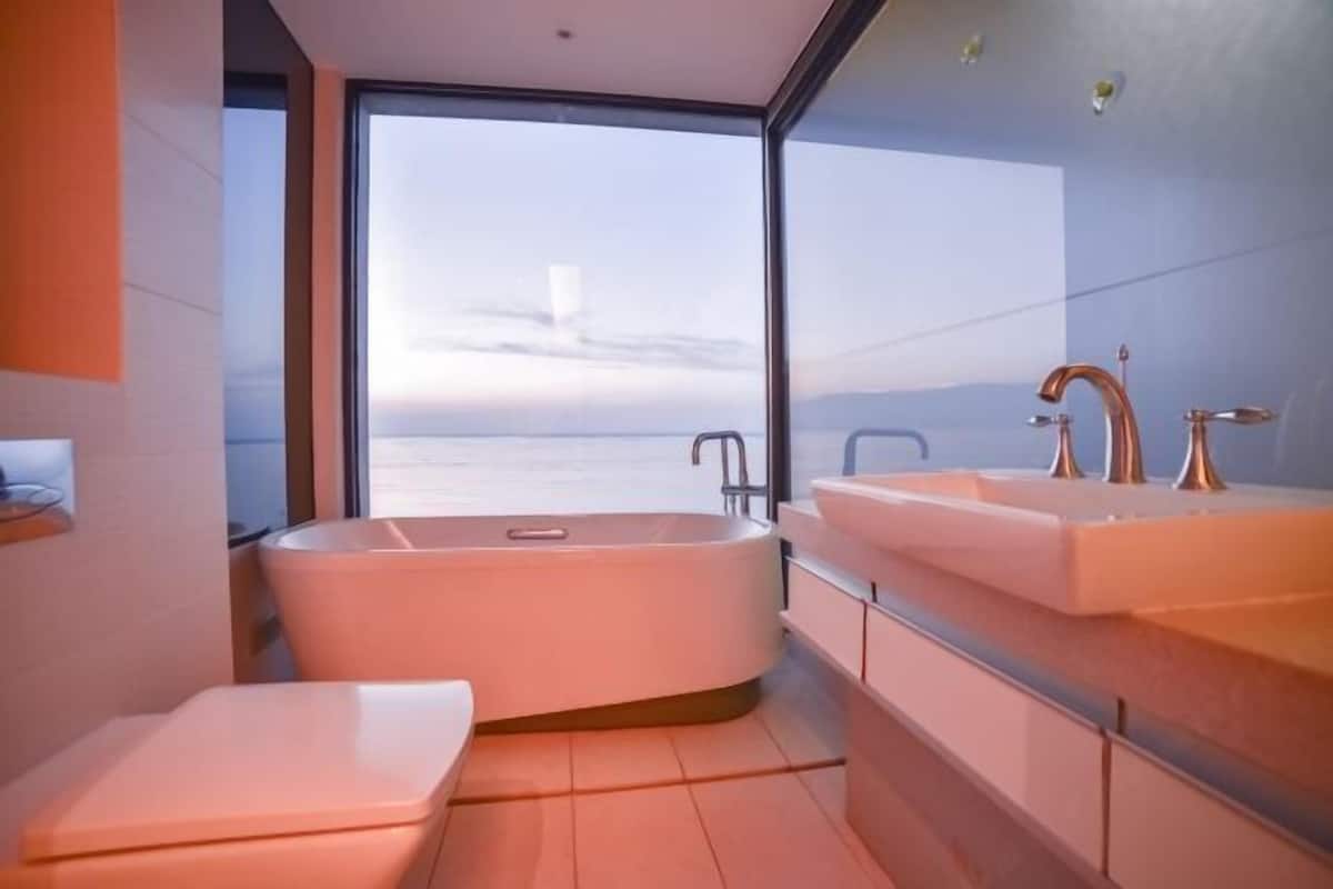 Um banheiro moderno com uma banheira grande, duas pias e vista para o mar.