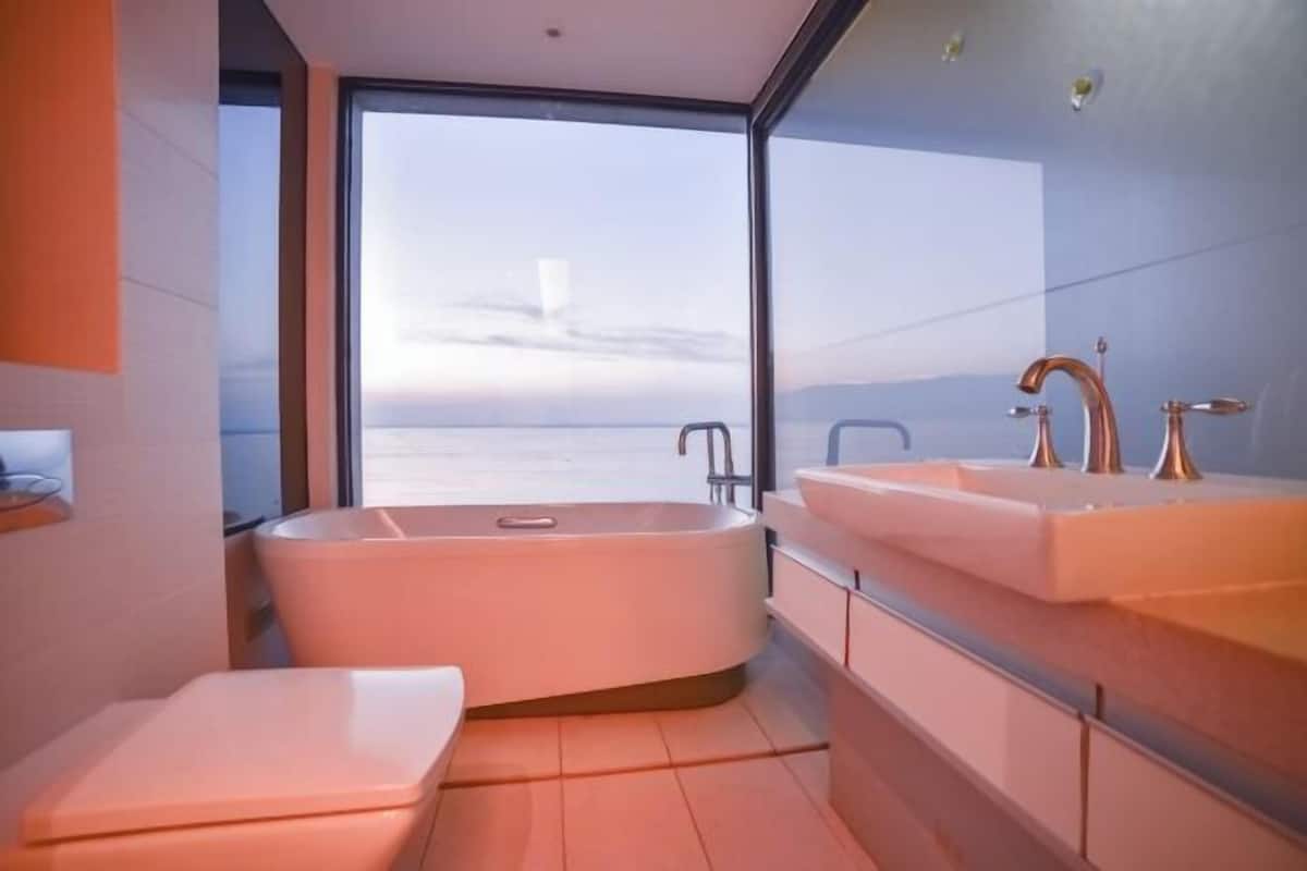 Um banheiro moderno com uma banheira grande, duas pias e vista para o mar.