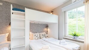 Quarto com cama beliche, janela com vista para vegetação e radiador.