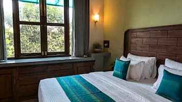 Quarto com cama grande, janela com cortinas, mesa de cabeceira com abajur e vista para árvores.
