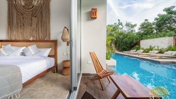 Quarto com cama, um painel de macramé na parede e uma cadeira de madeira à beira da piscina.