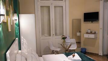 Quarto de hotel com cama, uma pequena mesa com cadeiras, televisão e espelho.