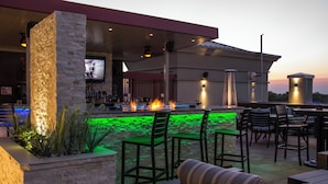 Um espaço de bar ao ar livre com pilares de pedra, iluminação ambiente verde e áreas de estar.