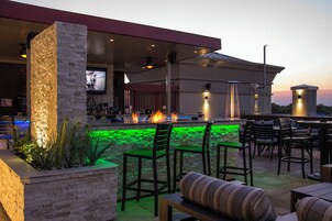 Um espaço de bar ao ar livre com pilares de pedra, iluminação ambiente verde e áreas de estar.