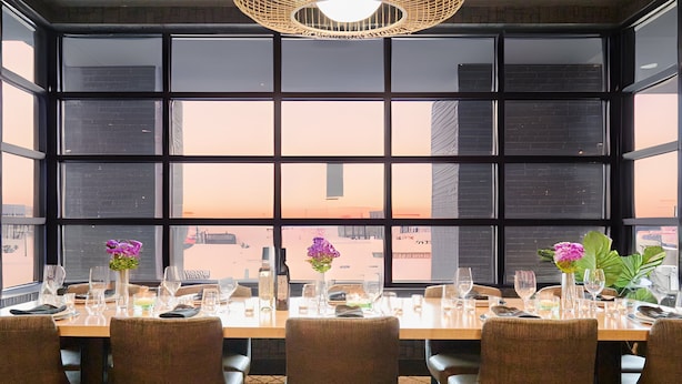 Mesa de jantar posta para seis pessoas, com vista para o pôr do sol através de grandes janelas.