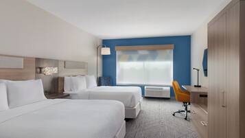 Quarto de hotel com duas camas, uma escrivaninha, uma cadeira, janela com persianas e ar condicionado fixado na parede.