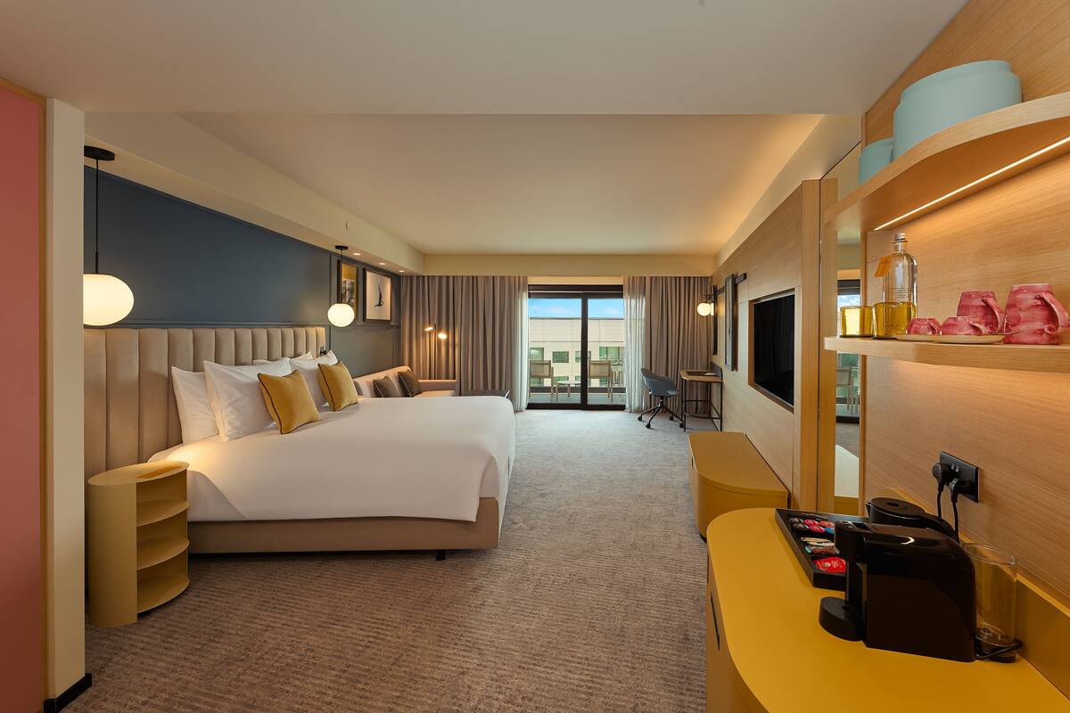 Quarto de hotel com cama grande, mesas de cabeceira, escrivaninha e televisão.