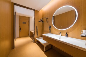 Um banheiro moderno com piso de madeira, pia branca, um espelho grande com iluminação circular e um porta-toalhas.