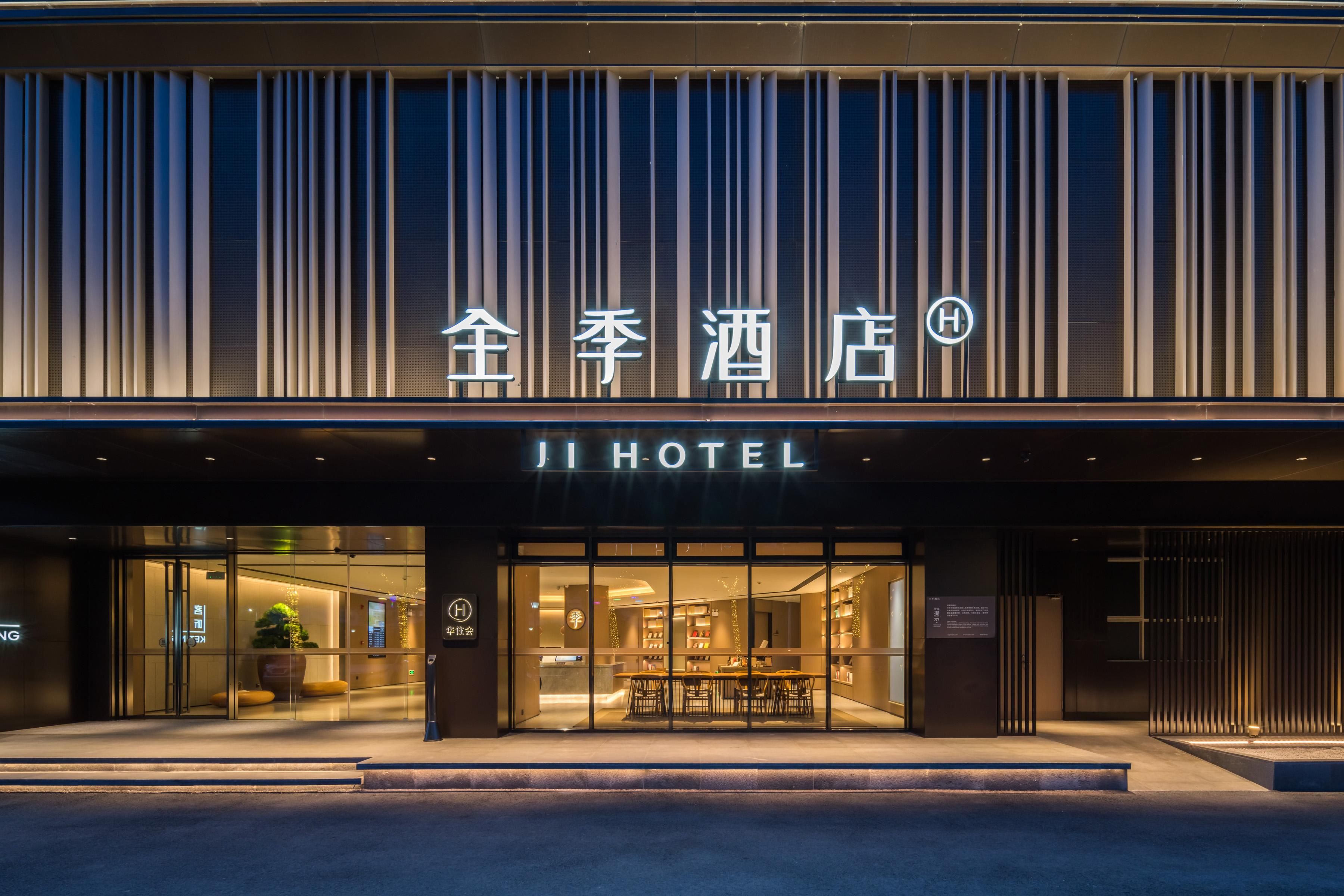 Entrada de hotel com ripas verticais e letreiros iluminados.