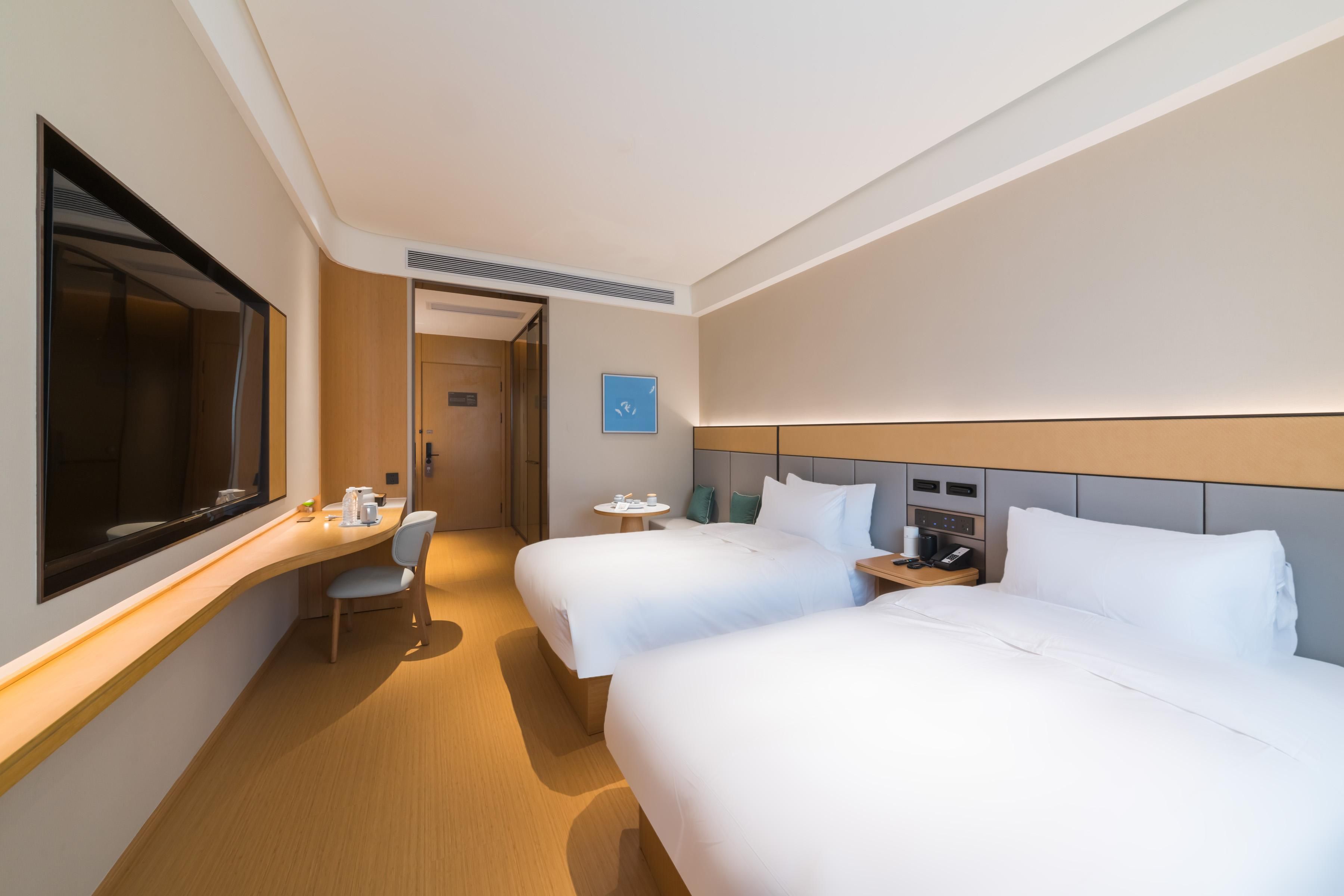 Quarto de hotel com duas camas, uma escrivaninha, uma cadeira, uma mesinha e uma televisão.