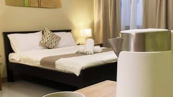 Quarto de hotel com cama, mesa de cabeceira com abajur e cafeteira grande.