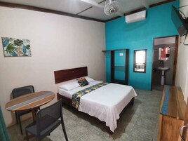 Quarto com cama, escrivaninha, cadeira, mesinha, ventilador e pia.