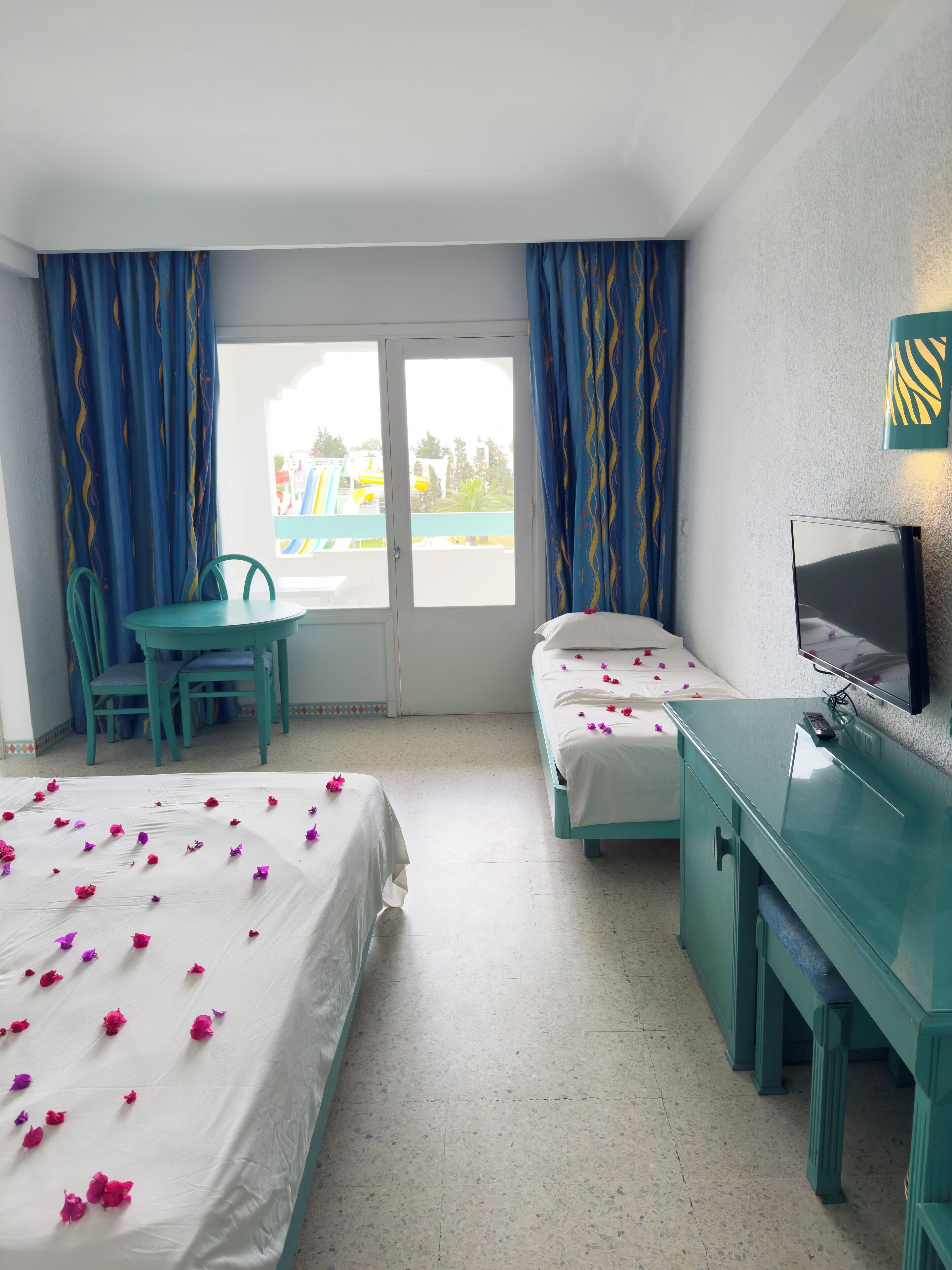 Quarto de hotel com duas camas, uma escrivaninha, uma cadeira e uma televisão.