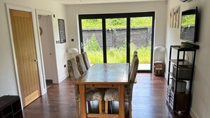 Um quarto espaçoso com uma mesa de jantar de madeira, cadeiras e uma televisão na parede.
