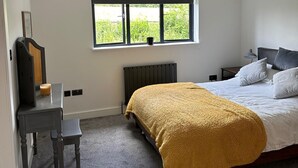 Quarto com teto inclinado, uma janela grande, uma cama com manta amarela, uma escrivaninha com cadeira e um radiador.