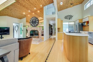 Uma sala de estar moderna com lareira, um relógio grande e uma área de cozinha com bancada e eletrodomésticos.