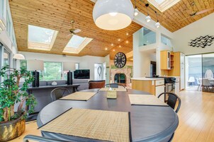 Uma sala de jantar espaçosa com teto alto, claraboias e uma cozinha moderna ao fundo.