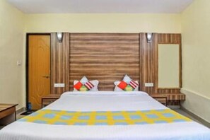 Quarto de hotel com cama, cabeceira de madeira, espelho e mesa de cabeceira.